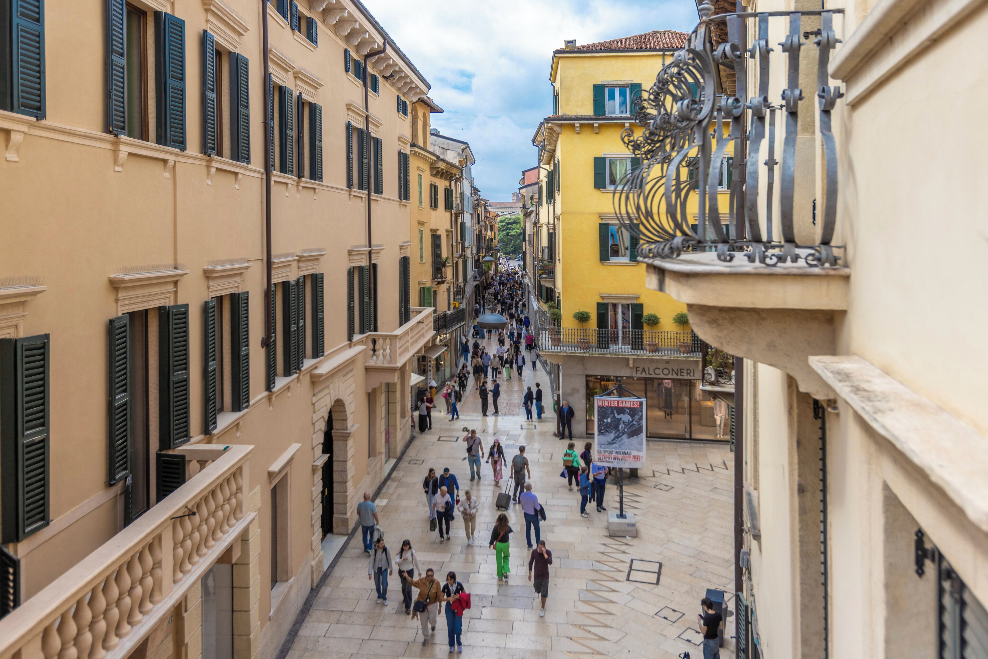 Rua para pedestres repleta de edifícios históricos, com uma multidão de pessoas e um letreiro chamativo para 'Water & Wine'.