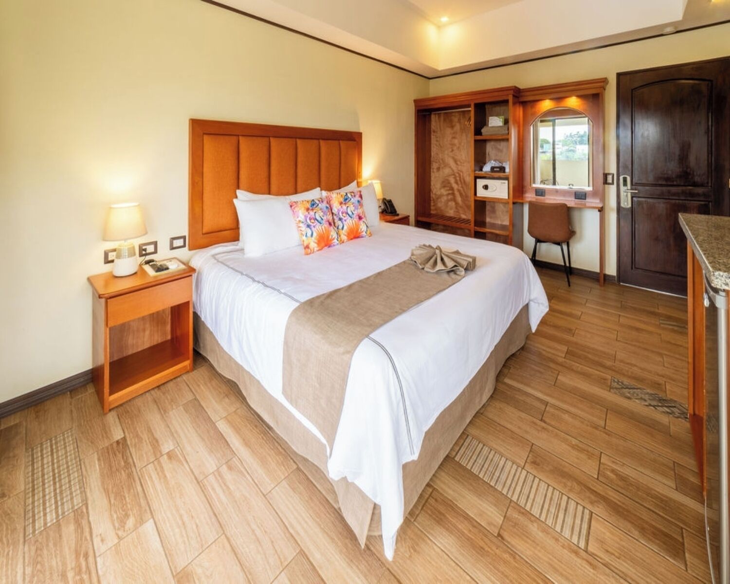 Quarto de hotel com cama grande, cabeceira de madeira, escrivaninha e guarda-roupa.