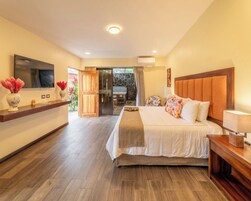 Quarto de hotel com uma cama grande, televisão, mesa consola de madeira e porta de vidro deslizante para uma área externa.