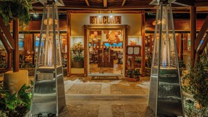 Entrada de um hotel com uma placa indicando "TOCUMA", apresentando um design moderno com teto de madeira e duas grandes estruturas metálicas em cada lado.