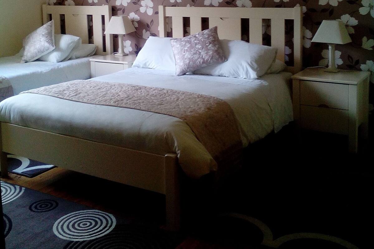 Uma cama de casal com peseira de madeira, duas mesas de cabeceira com luminárias e papel de parede estampado com flores.