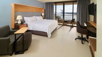 Quarto de hotel com cama, escrivaninha, cadeira e vista para um corpo de água.