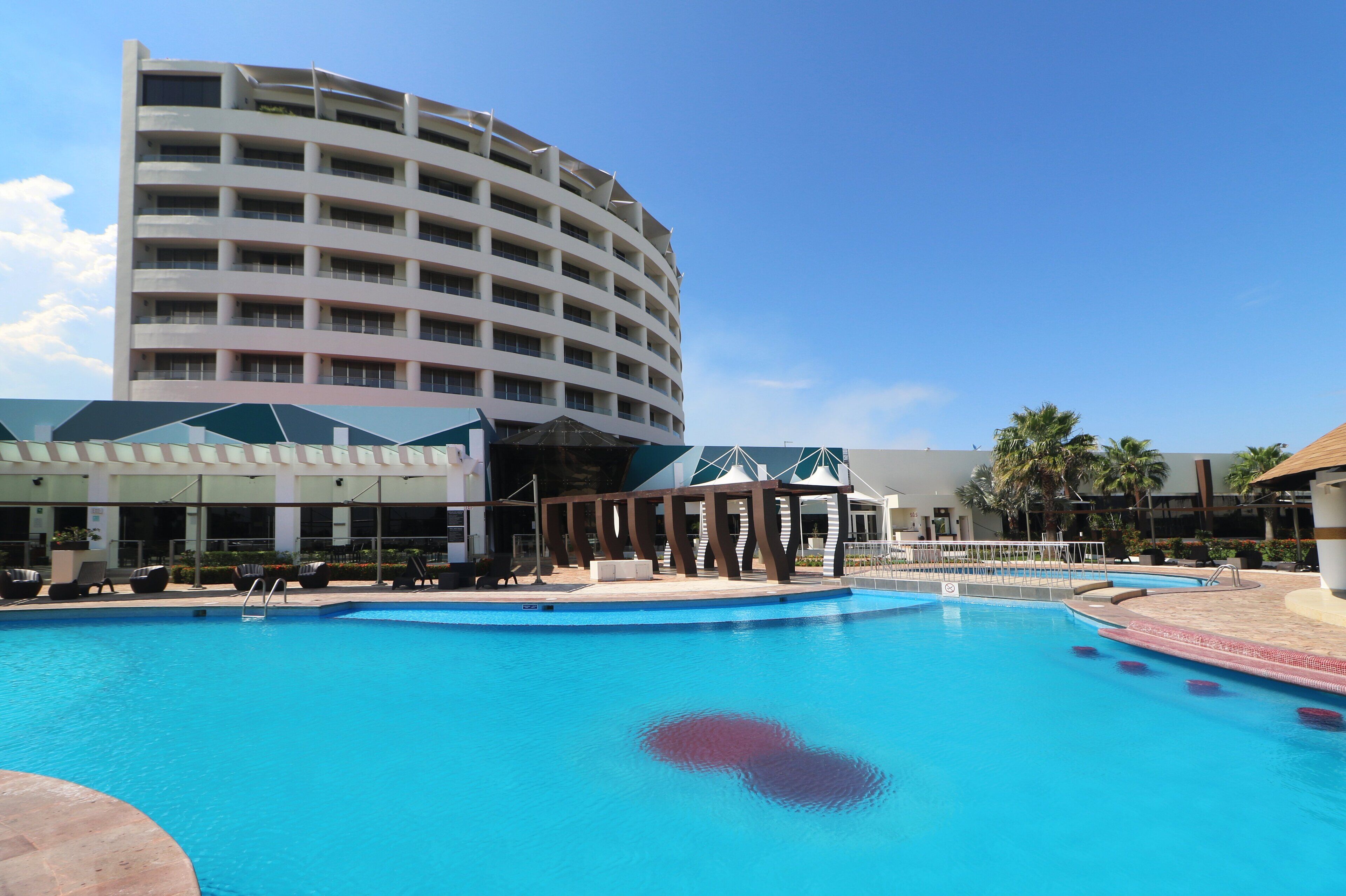 Um hotel com uma piscina grande, um edifício curvo e áreas de estar ao ar livre.
