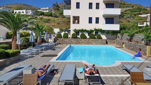 Área da piscina com espreguiçadeiras, piscina e um edifício moderno ao fundo.