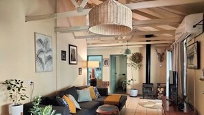 Uma sala de estar aconchegante com sofá, mesa de centro e luminária pendente. Há uma lareira e uma televisão sobre um suporte de madeira.