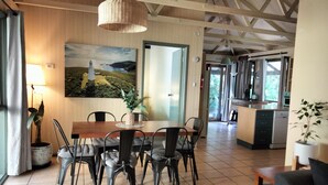 Uma área de refeições com mesa e cadeiras de madeira, um lustre e uma pintura de paisagem.