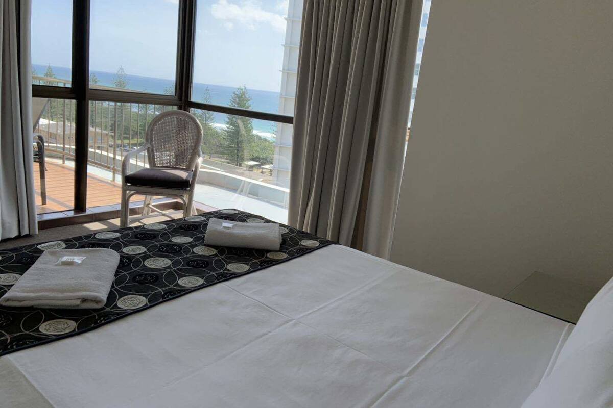 Quarto de hotel com uma cama, uma cadeira e vista para o oceano.