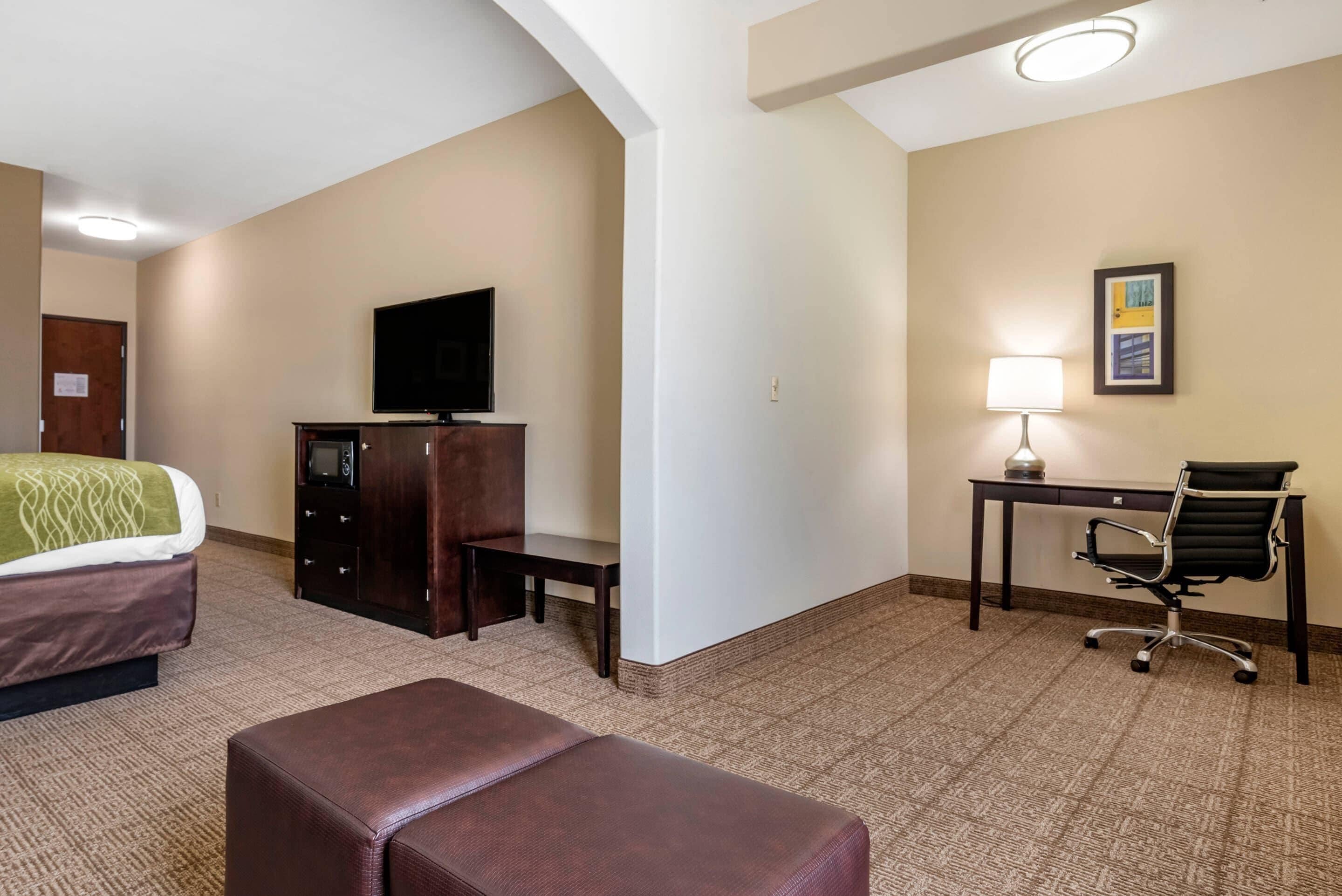 Quarto de hotel com uma cama, uma escrivaninha com cadeira, televisão e abajur.