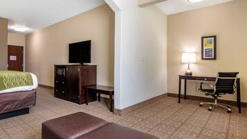 Quarto de hotel com uma cama, uma escrivaninha com cadeira, televisão e abajur.