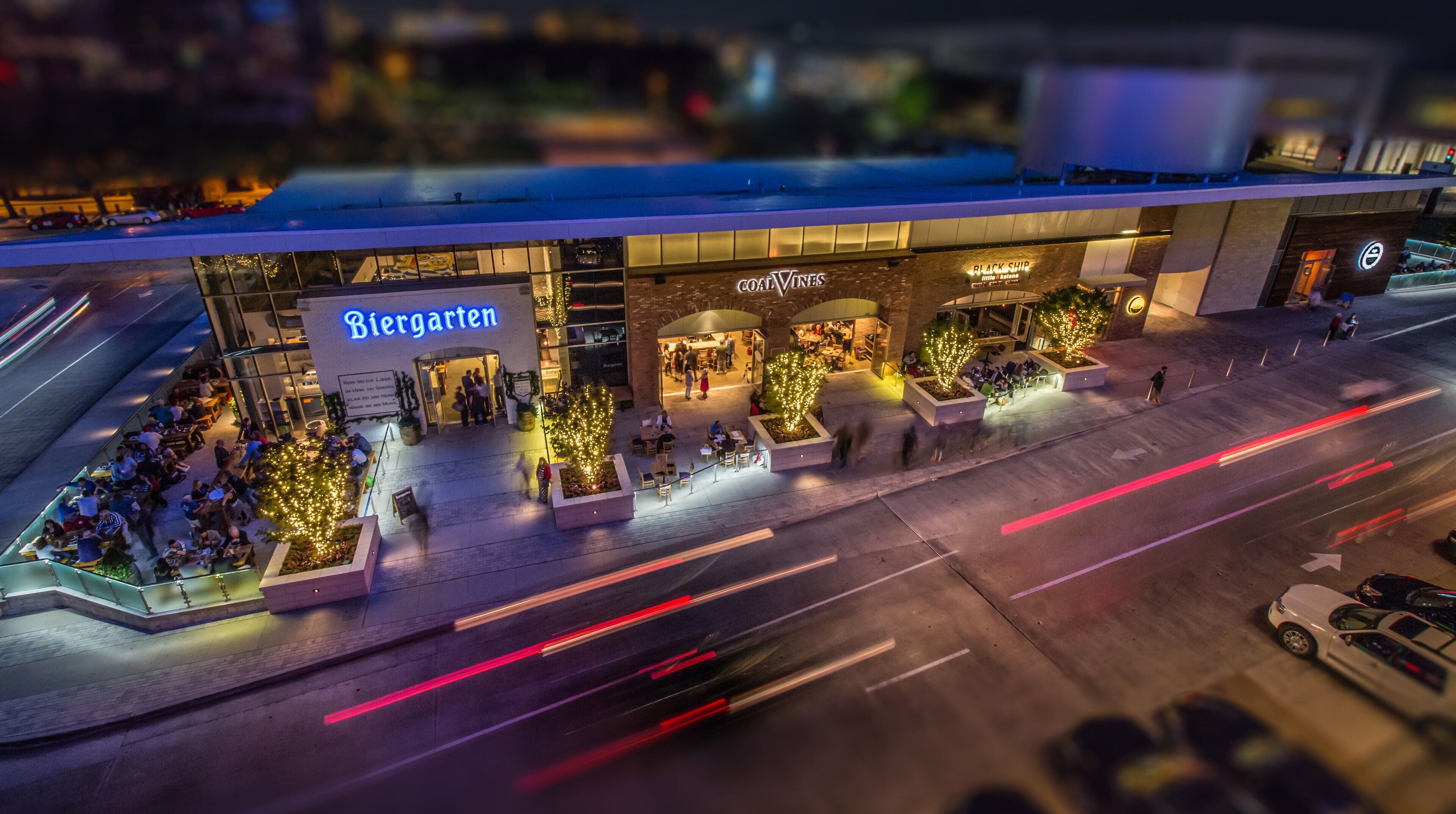 Vista aérea do Biergarten com mesas ao ar livre e entrada bem iluminada.