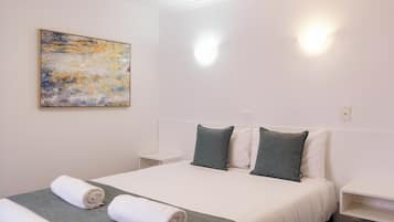 Quarto de hotel com uma cama, duas almofadas, um quadro na parede e uma mesinha de cabeceira.