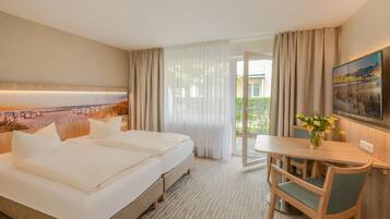 Quarto de hotel com cama, escrivaninha e cadeira. Há uma janela com cortinas e vista para o exterior.