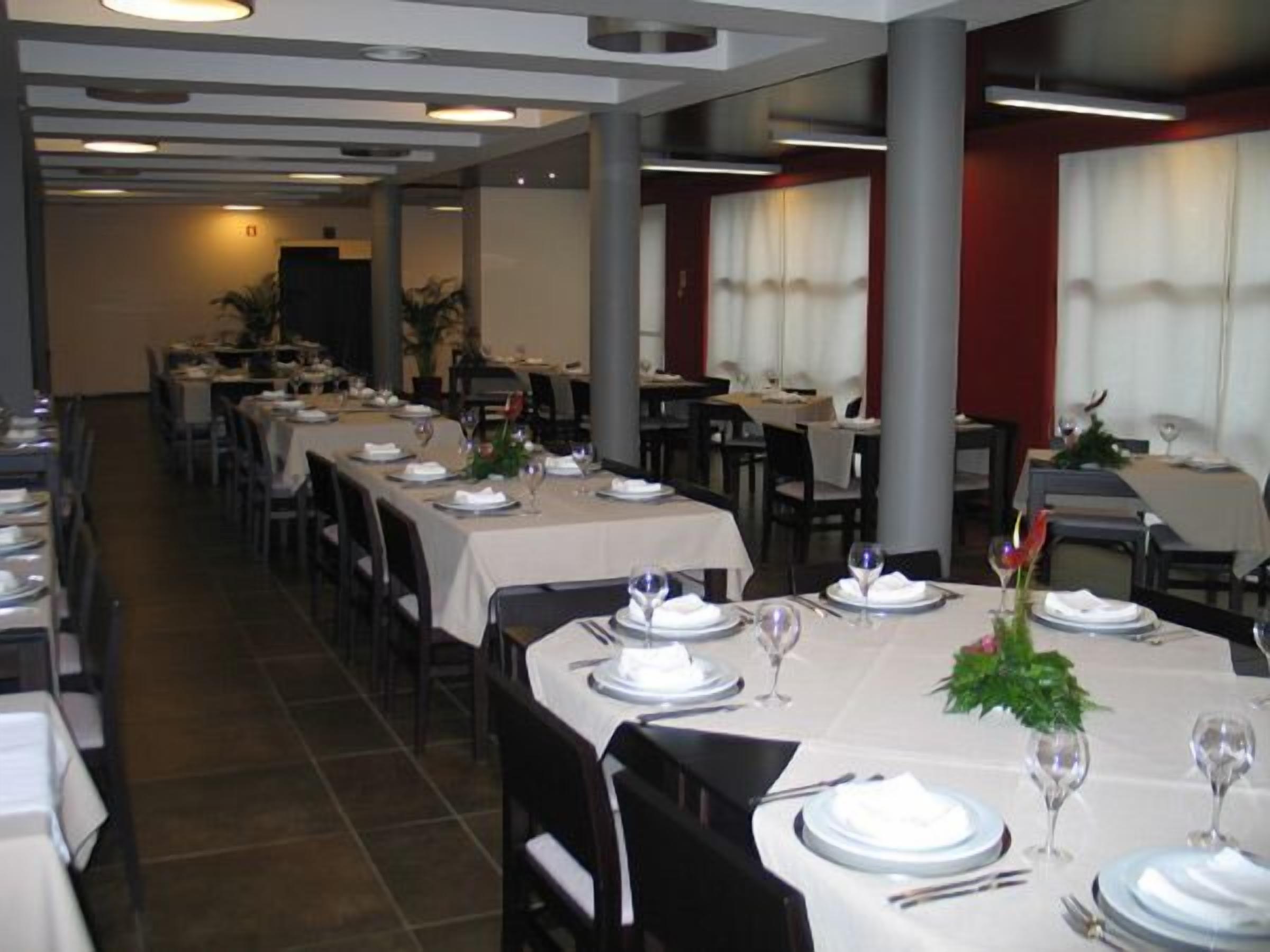 Uma sala de jantar espaçosa com várias mesas postas para refeições, com toalhas brancas e pratos e copos bem arrumados.
