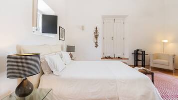 Quarto com cama, mesa de cabeceira com abajur, uma cadeira e uma porta.