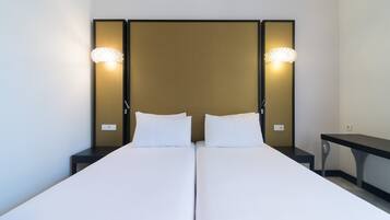 Cama de casal com roupa de cama branca, duas mesas de cabeceira com abajures e cabeceira com design texturizado.