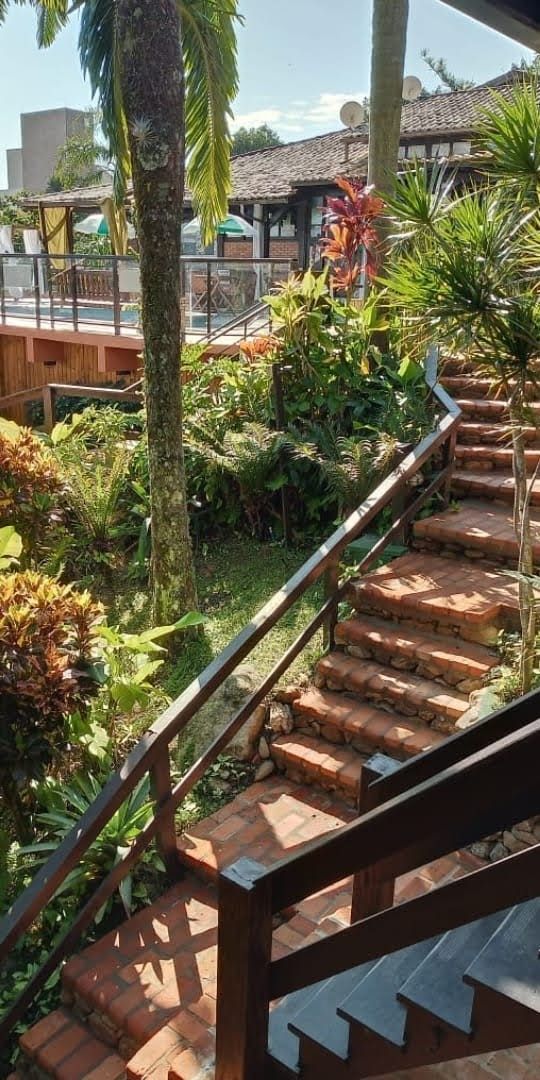 Escadaria com corrimão metálico que leva a uma área coberta, com plantas e vista para edifícios ao fundo.