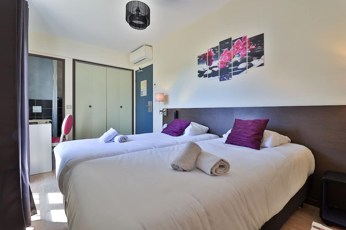 Quarto de hotel com duas camas, um guarda-roupa, uma escrivaninha e um espelho.