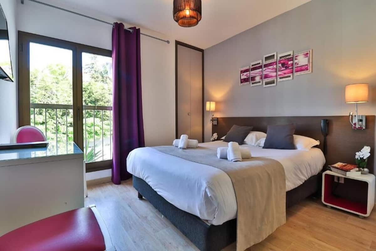 Quarto de hotel moderno com uma cama grande, uma mesa de trabalho e uma varanda com vista.