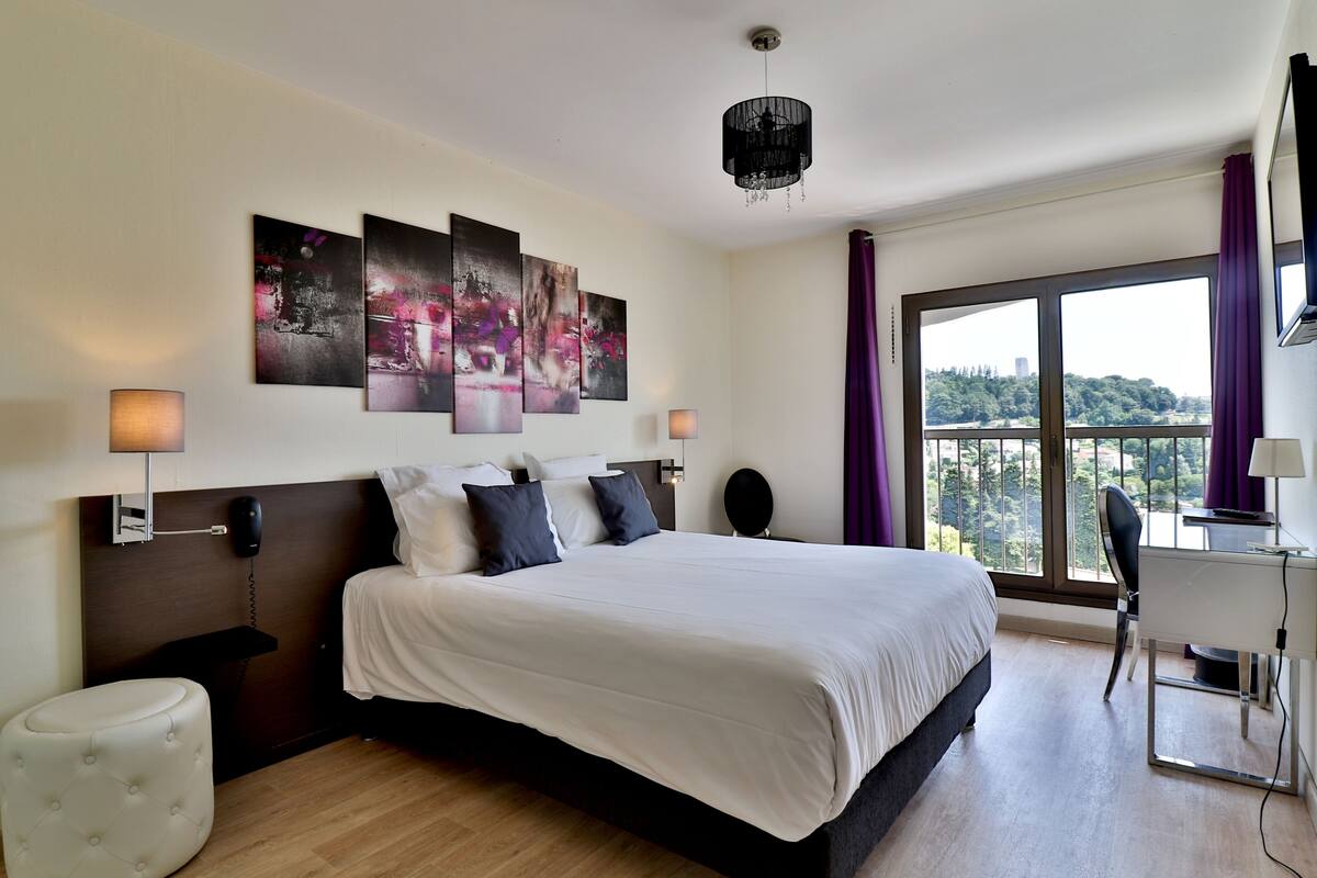 Quarto de hotel moderno com uma cama grande, uma escrivaninha e vista para a cidade.