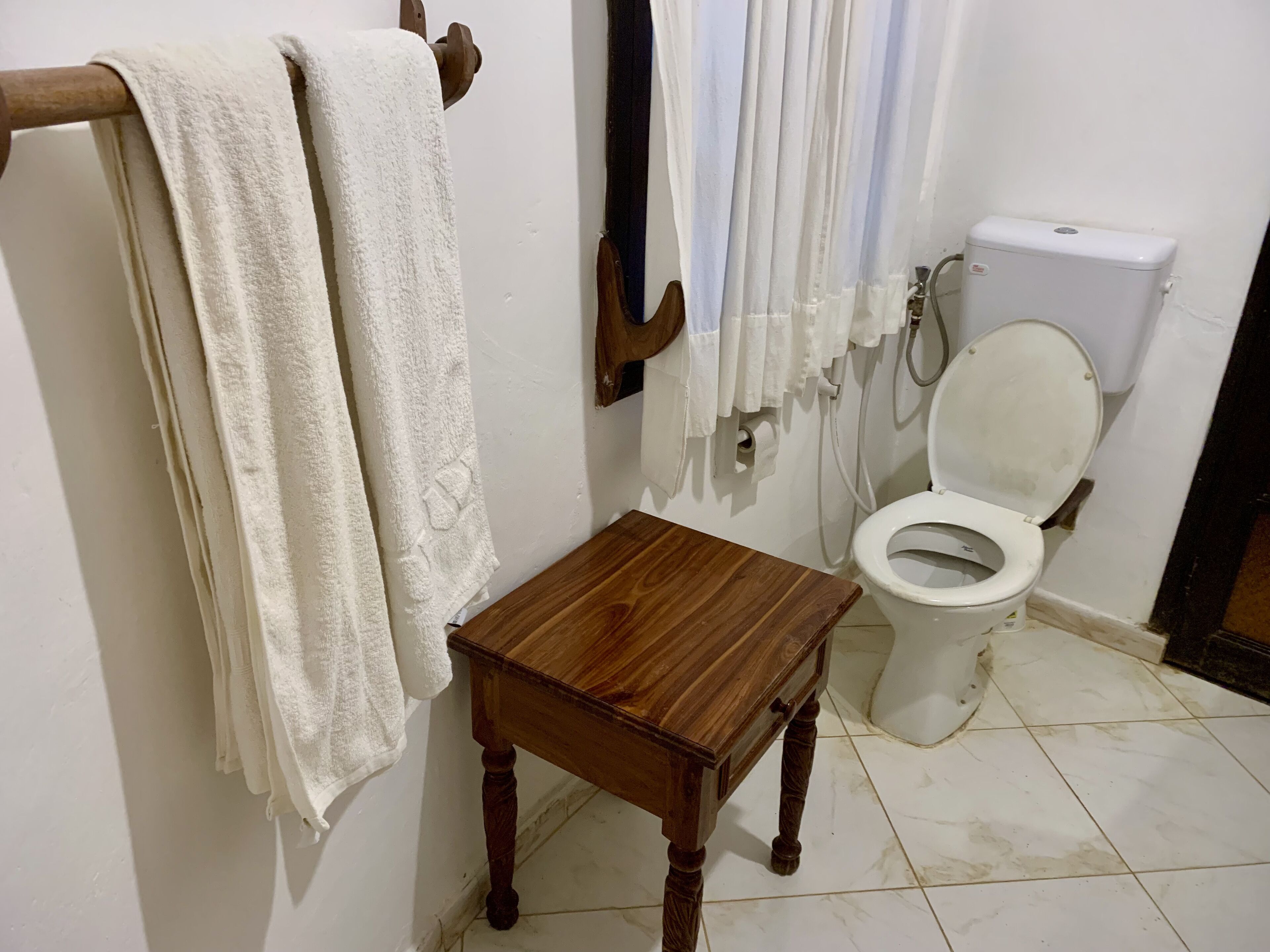 Um banheiro com um banquinho de madeira, vaso sanitário e porta-toalhas com toalhas.