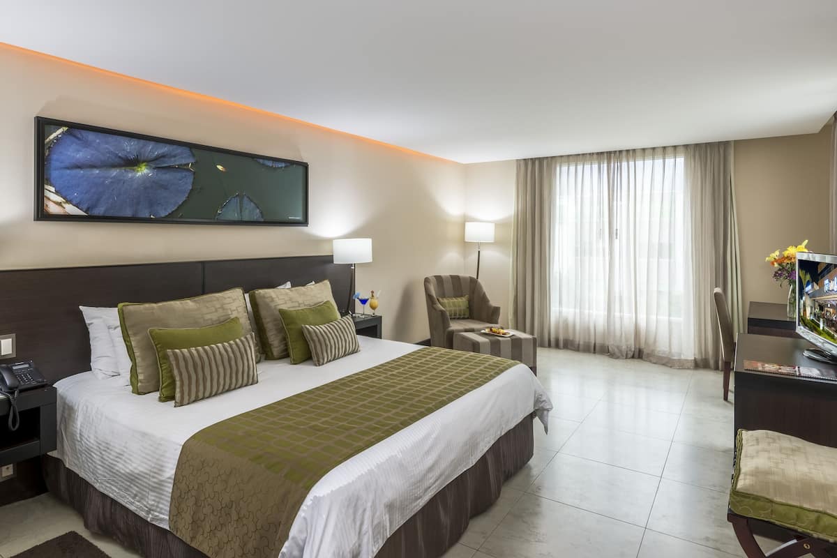 Quarto de hotel com uma cama grande, uma escrivaninha com computador, uma cadeira e uma televisão.