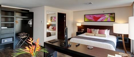 Quarto de hotel com cama, mesas de cabeceira, escrivaninha, cadeira, guarda-roupa e espelho.
