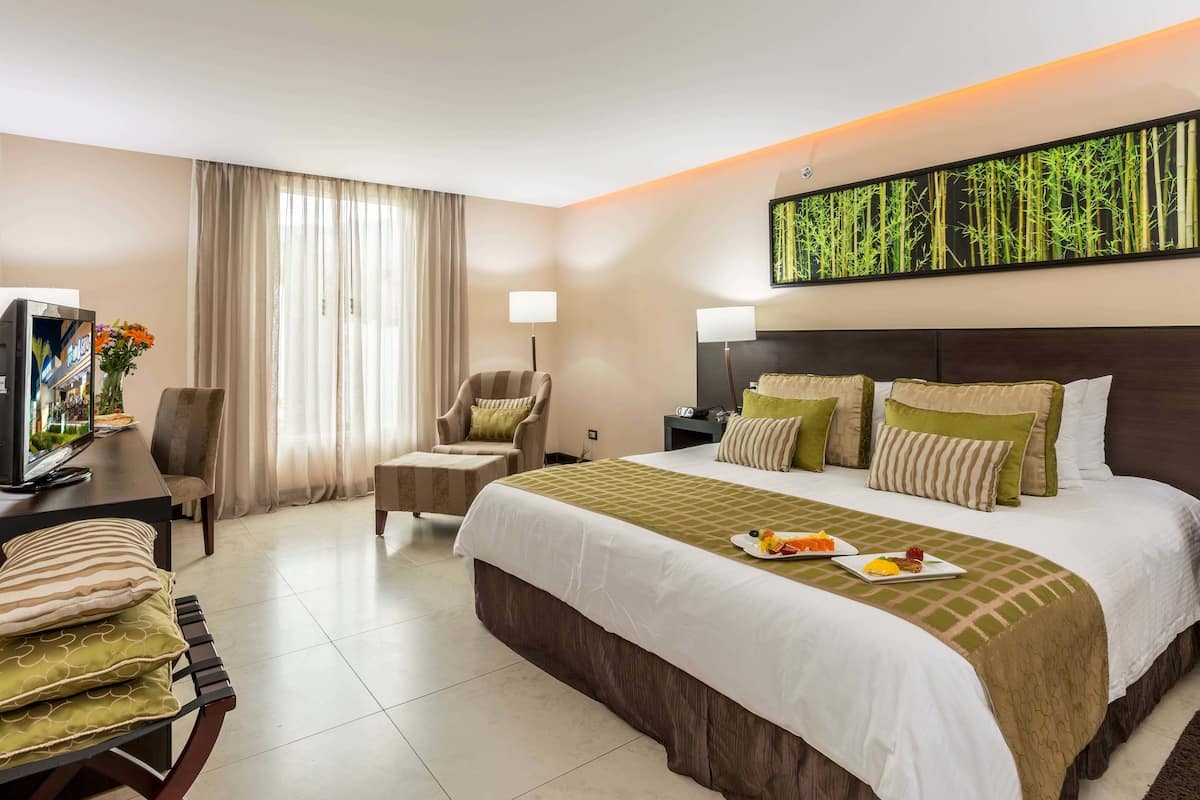 Quarto de hotel com uma cama grande, televisão, escrivaninha com computador e uma cadeira.