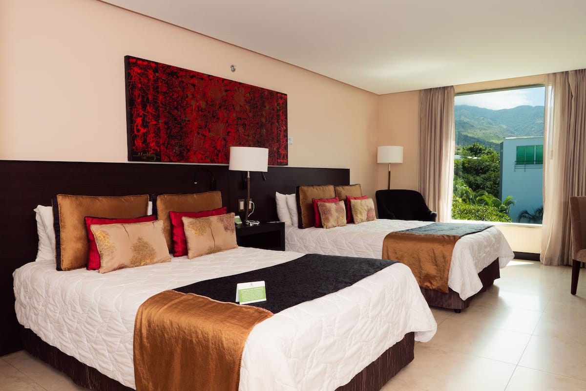 Quarto de hotel com duas camas, uma janela grande e uma pintura abstrata vermelha na parede.