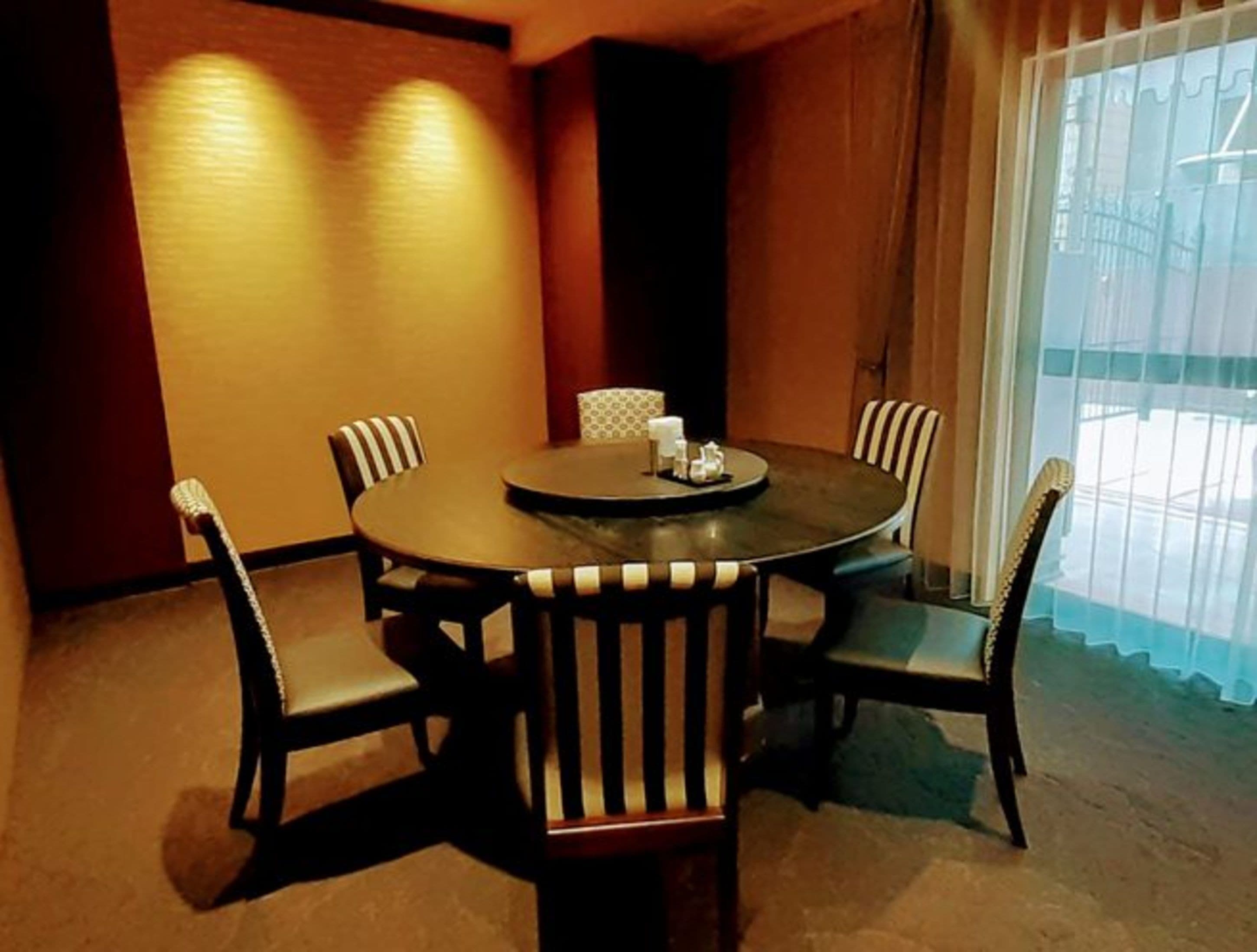Mesa de jantar redonda com quatro cadeiras, um pequeno tabuleiro com objetos e uma janela com cortinas.