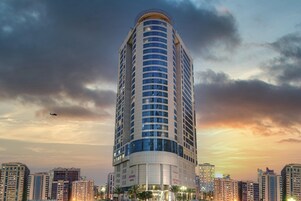 Um hotel moderno e imponente, com fachada curva, vários andares e entrada destacada na base.