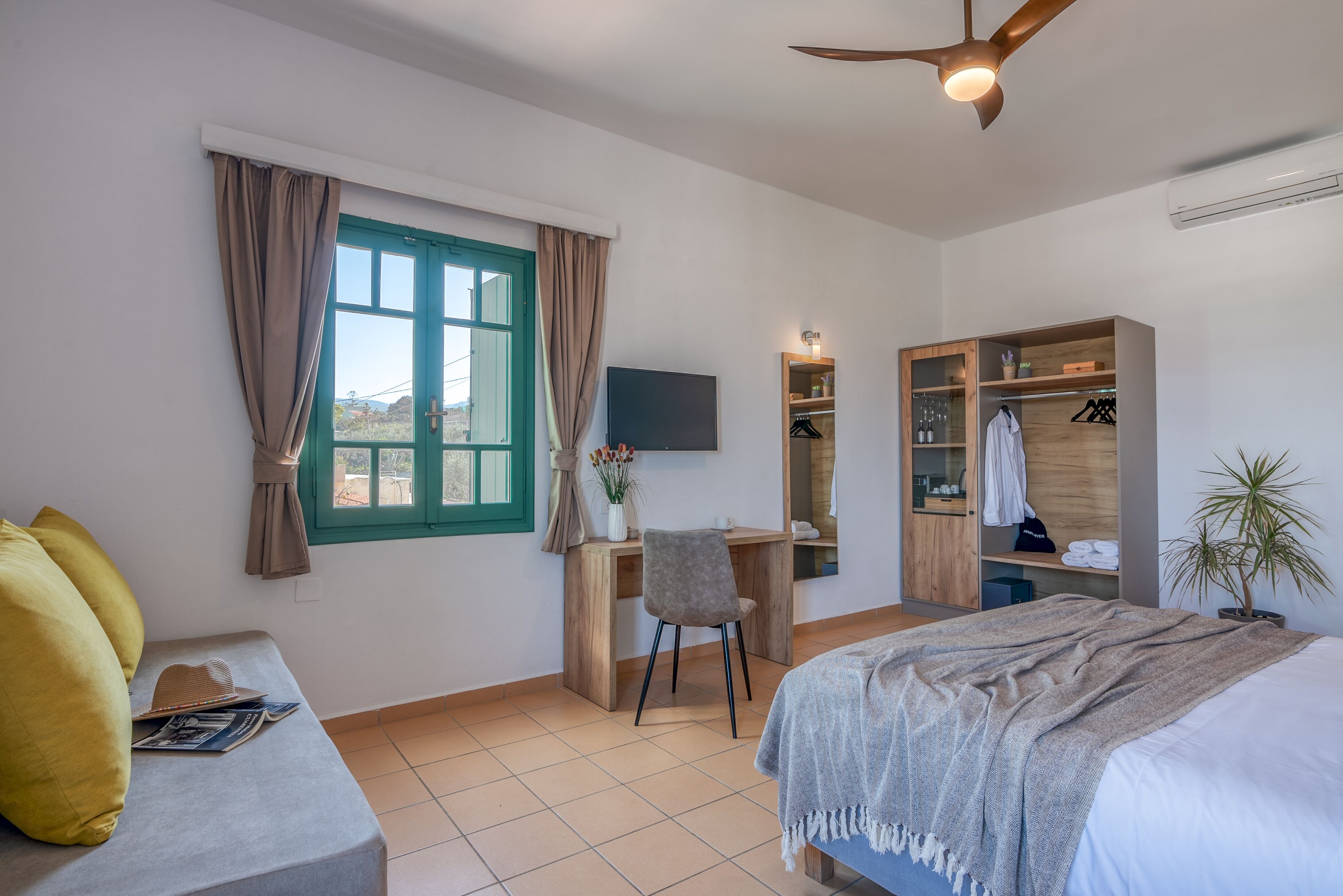 Quarto com cama, escrivaninha, cadeira, guarda-roupa, televisão e janela com cortinas.