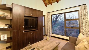 Uma sala de estar com um armário de madeira escura, uma televisão de tela plana, uma mesa de centro com revistas e um sofá.