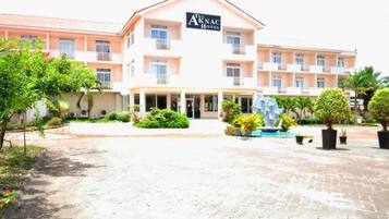 Hotel com vários andares, entrada central, varandas e um pátio ajardinado.