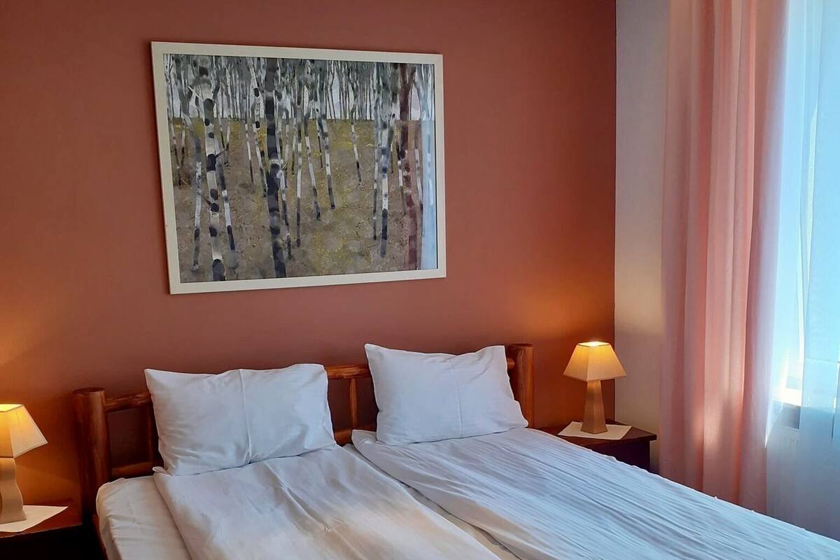 Uma cama de casal bem arrumada com lençóis brancos, duas luminárias de cabeceira e um quadro na parede.