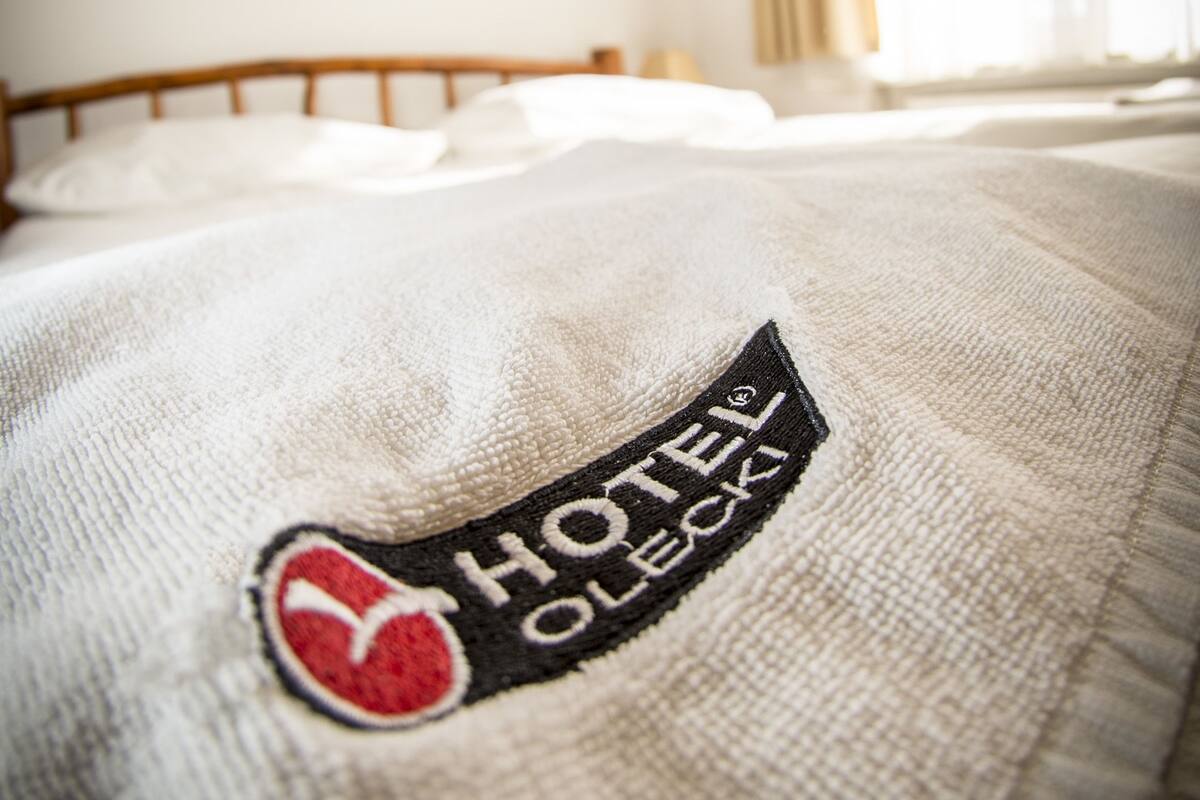 Uma cama de hotel com o logotipo Hotel Oleodok, uma cabeceira de madeira e um quadro na parede.