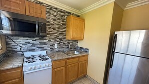 Cozinha com armários de madeira, geladeira de aço inoxidável, micro-ondas, fogão e painel de azulejos.