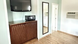 Quarto com televisão de tela plana fixada em um armário de madeira, espelho fixado na parede e porta branca.
