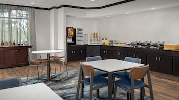 Quarto de hotel moderno com área de refeições, cozinha com estação de café e uma grande janela com cortinas.