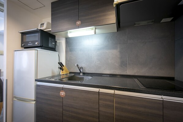 Cozinha compacta com micro-ondas, geladeira, pia e armários de madeira escura.