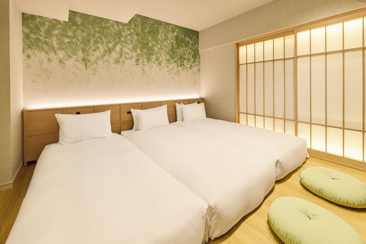 Quarto de hotel com uma cama grande, cabeceira de madeira, parede verde e um shoji.