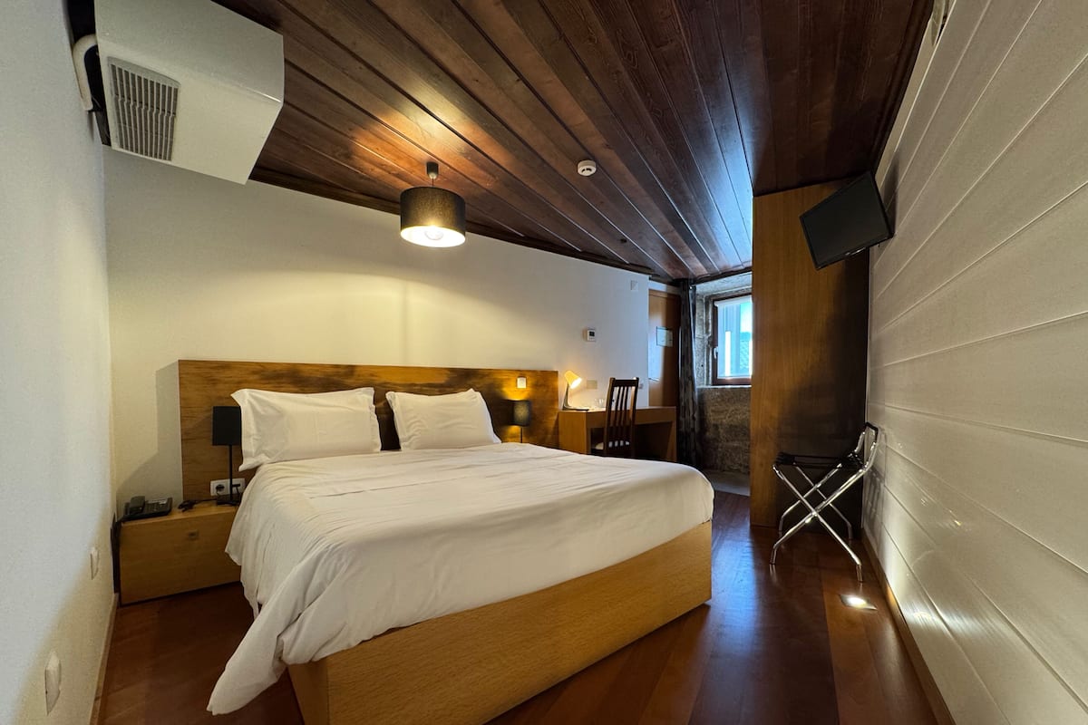 Quarto com cama de madeira, mesas de cabeceira, escrivaninha e uma cadeira.