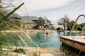 Área de piscina com água cristalina, espreguiçadeiras, guarda-sóis e um deck de madeira.