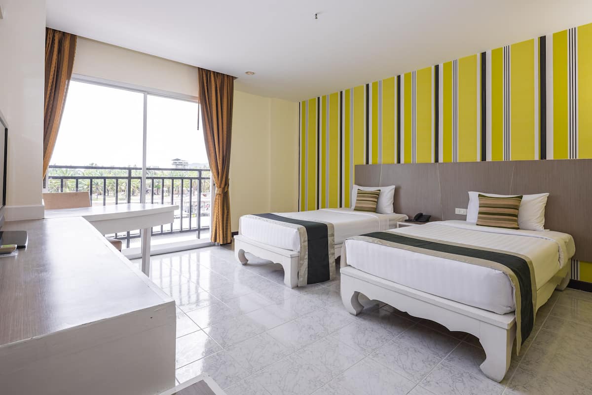 Quarto de hotel com duas camas, uma mesa de trabalho e varanda com cortinas.