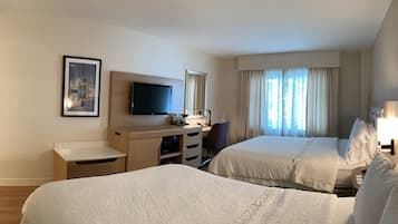 Quarto de hotel com duas camas, uma secretária com computador, televisão e janela com cortinas.