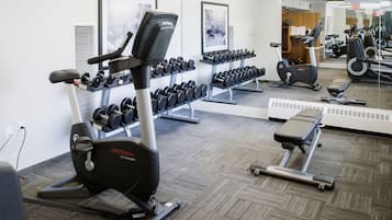 Uma academia com equipamentos de cardio, halteres e bancos.