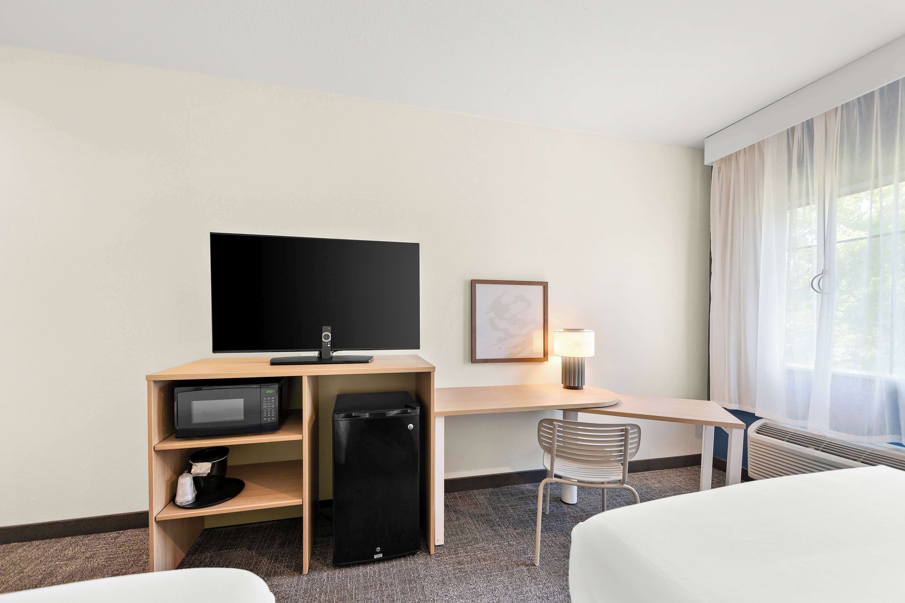Quarto de hotel com TV de tela plana, micro-ondas, mini-geladeira, escrivaninha, cadeira e cama.