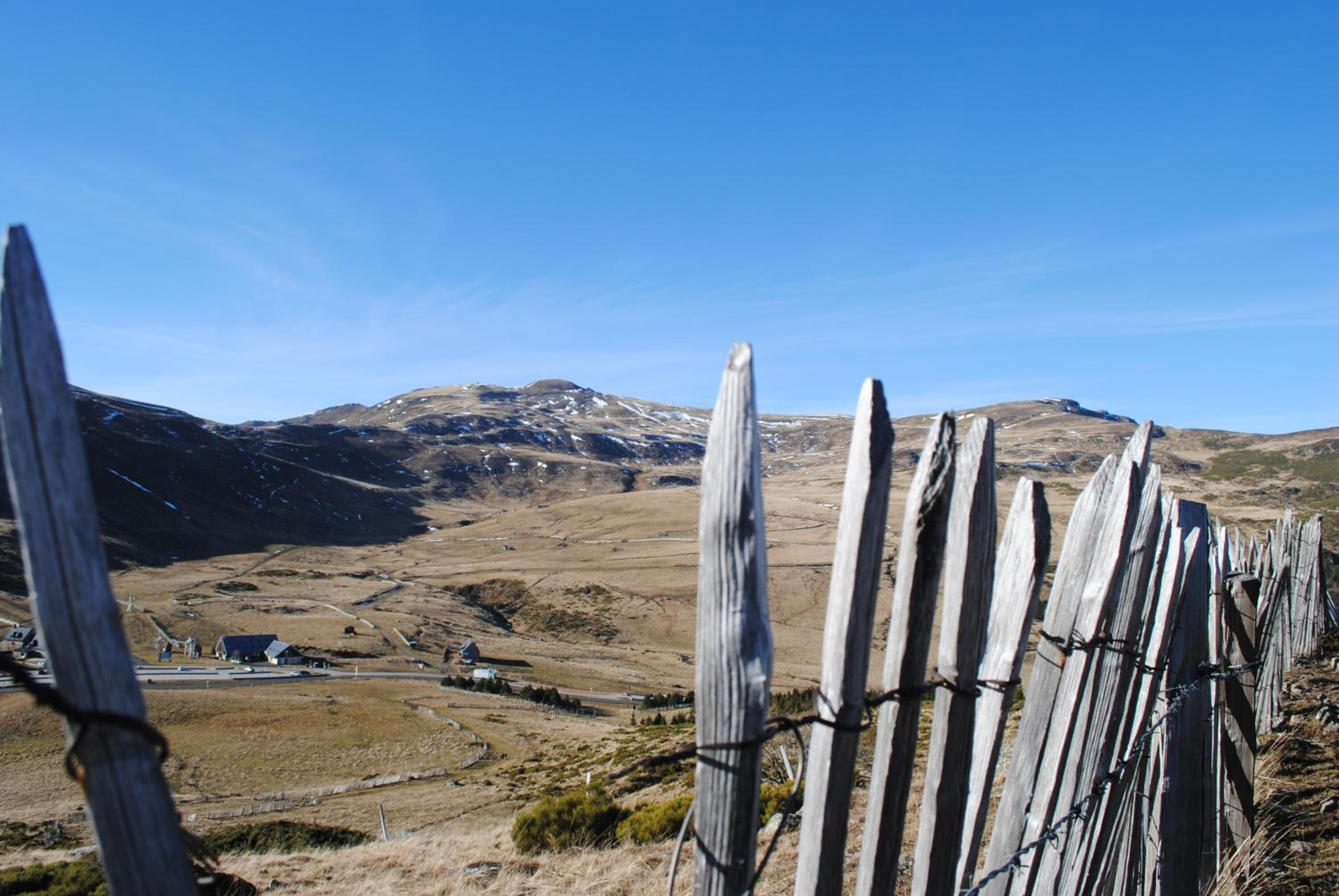 Paisagem rural com cerca de madeira, montanha distante e alguns edifícios no vale.