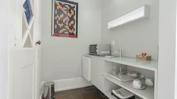 Uma cozinha compacta com micro-ondas, um refrigerador pequeno e uma estante de vidro com louças.