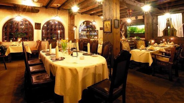 Restaurante com interiores em madeira, mesas redondas e ambiente iluminado por velas.