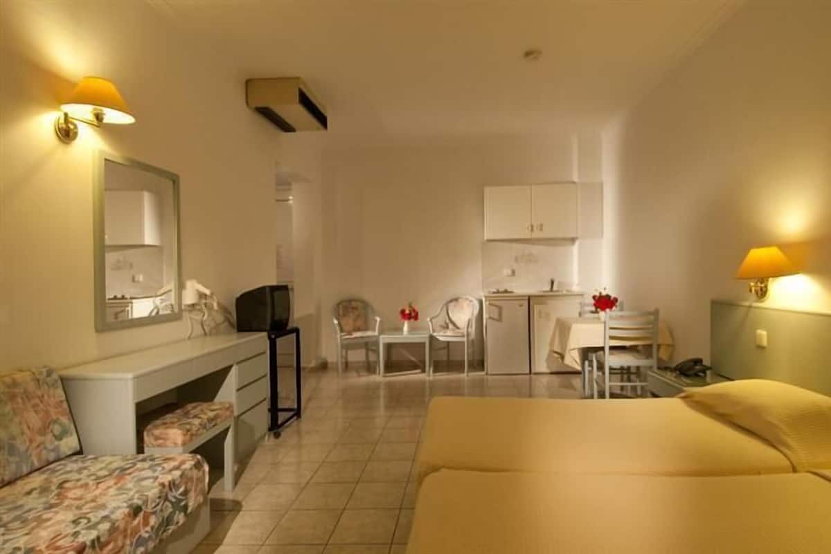 Quarto de hotel com uma cama, uma escrivaninha, uma cadeira, uma mesinha e uma kitchenette.